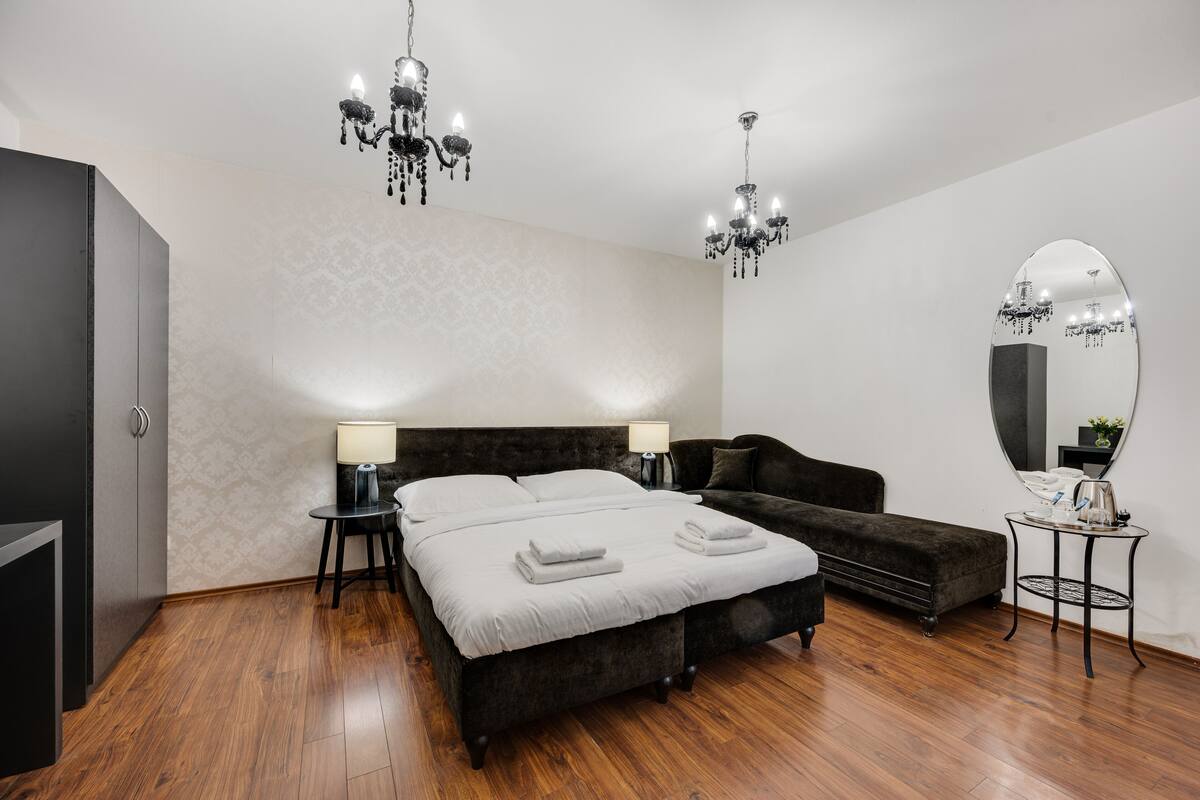 Quarto com uma cama grande, duas mesas de cabeceira, um sofá escuro, um espelho redondo e um lustre.
