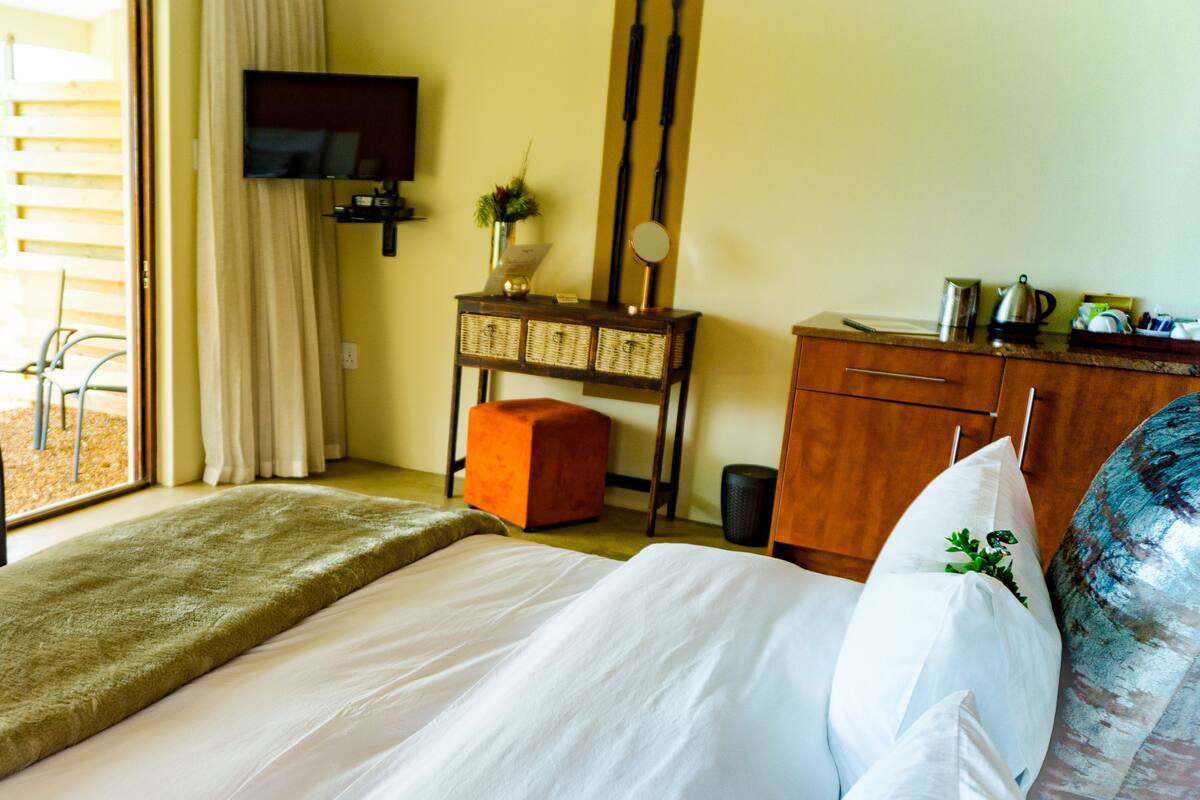 Quarto de hotel com uma cama, uma cadeira, uma mesinha e uma televisão na parede.