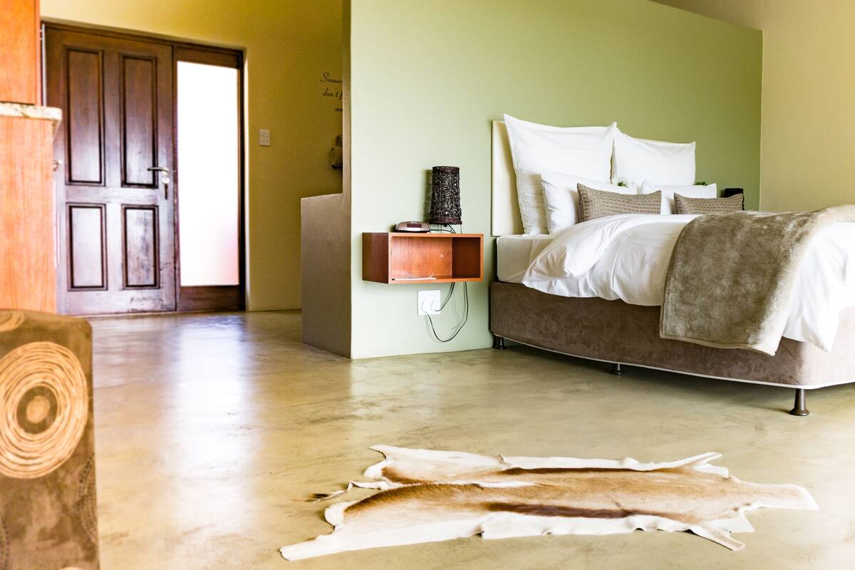 Quarto com cama, mesa de cabeceira e luminária na parede.