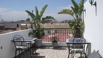 Uma varanda com duas mesas e cadeiras, plantas em vasos e vista para a paisagem urbana.