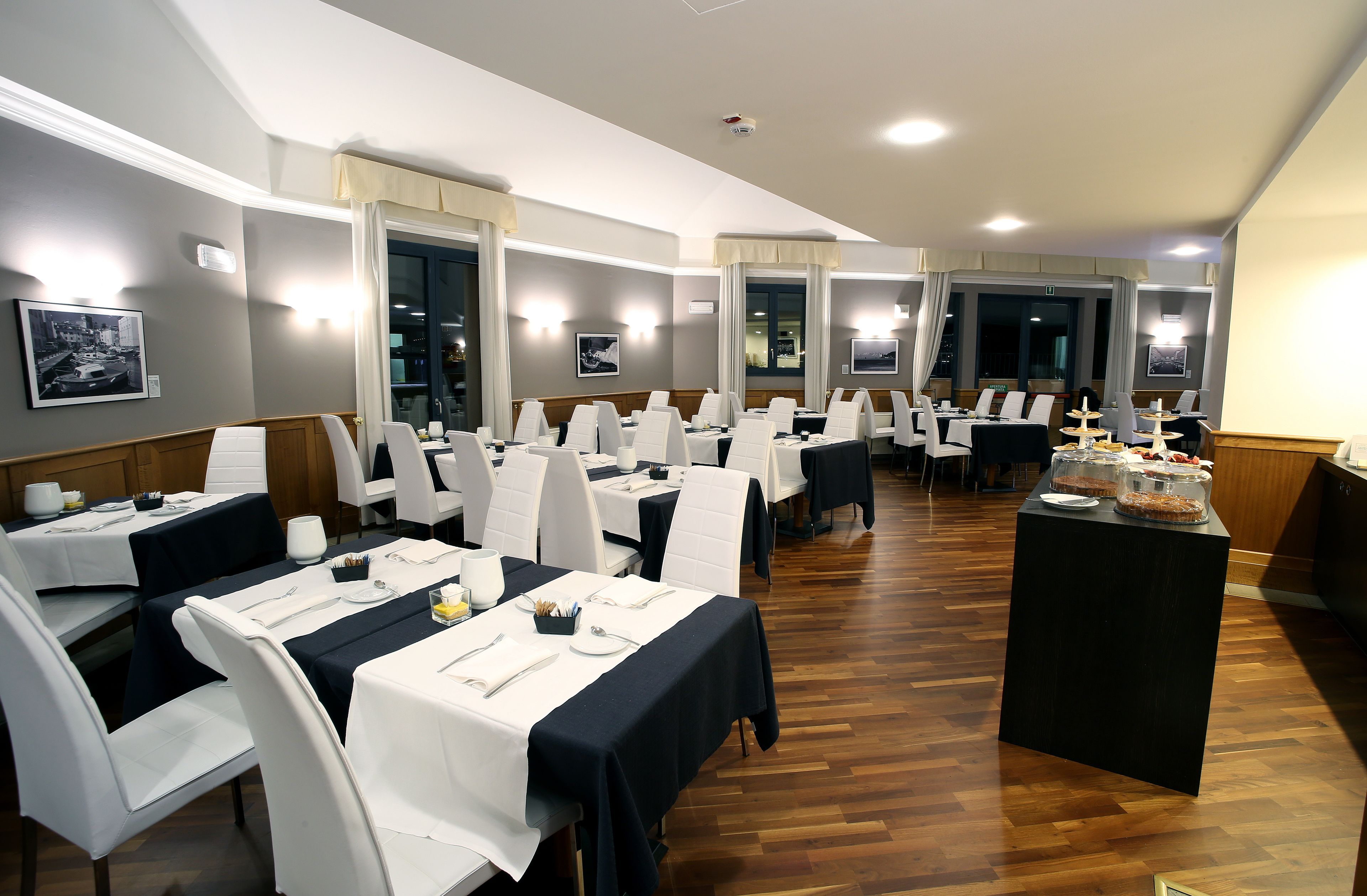 Sala de conferências com várias mesas dispostas para refeições, equipada com cadeiras brancas e toalhas de mesa pretas.