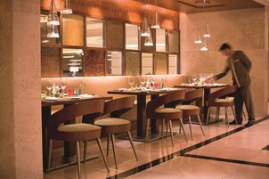 Restaurante com interior moderno, com mesas e cadeiras de madeira e iluminação pendente.