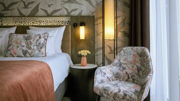Quarto de hotel com cama, cadeira, mesa de cabeceira, luminária na parede e painel decorativo.