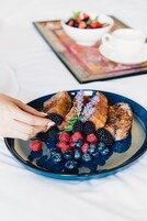 Uma fatia de pão com ovos e frutas vermelhas, acompanhada de um ramo de lavanda, sobre um prato azul.