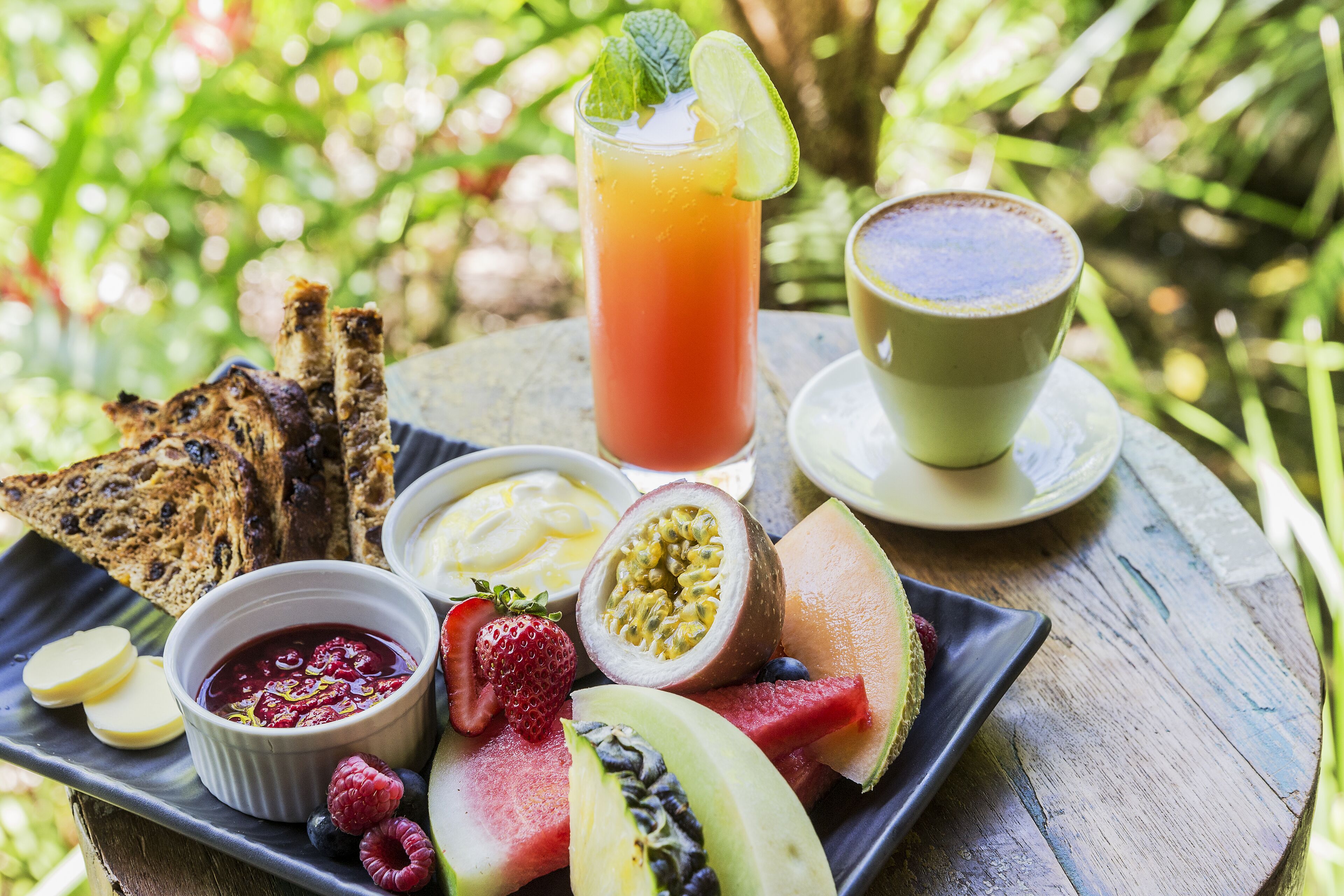 Uma bandeja de café da manhã com torradas, frutas, iogurte e uma bebida sobre uma mesa de madeira.