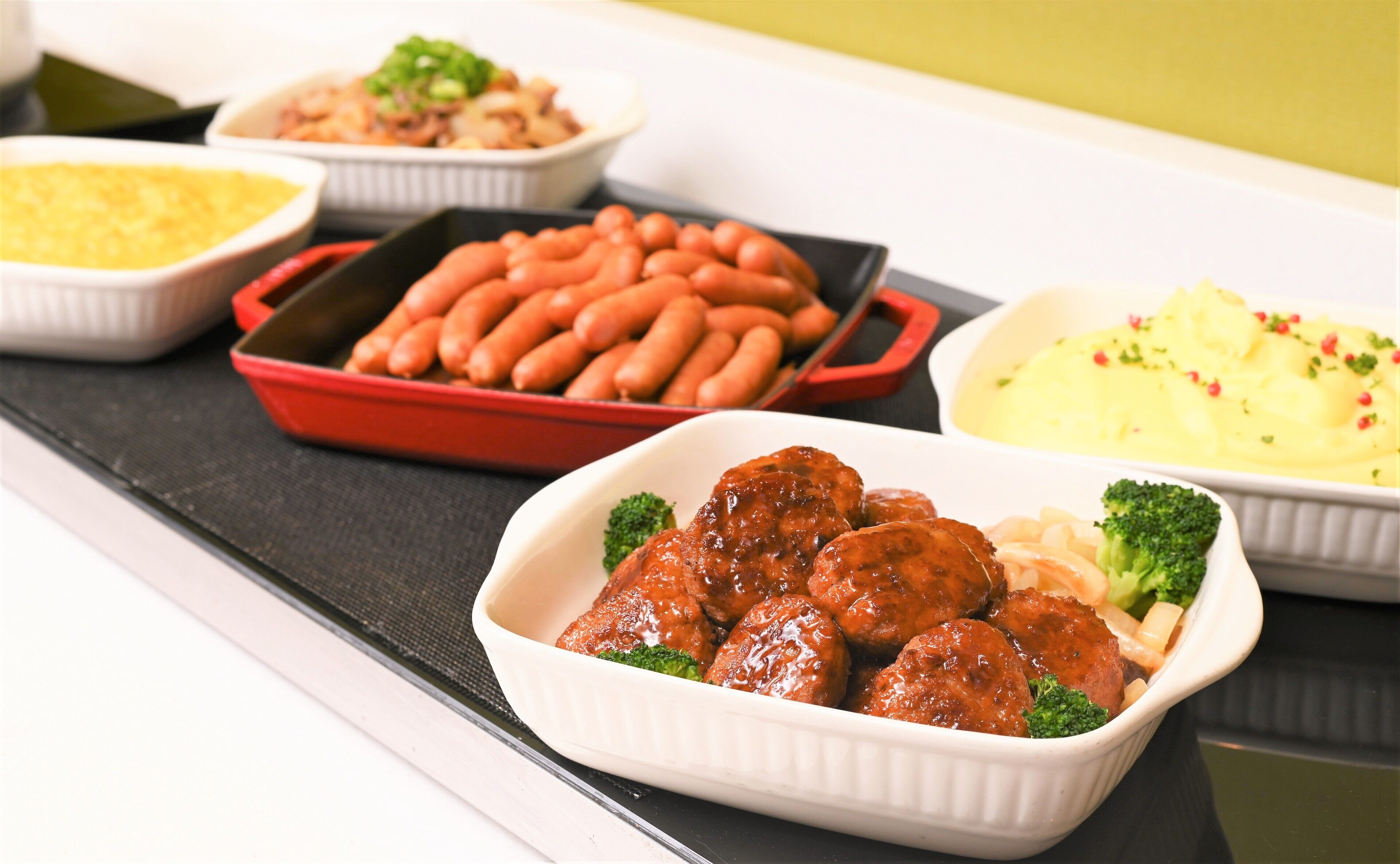 Uma mesa com vários pratos, incluindo salsichas, purê de batatas e almôndegas.
