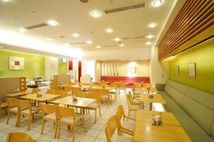 Uma sala de jantar ampla com várias mesas e cadeiras, um espaço de assentos em cabine vermelho e uma parede de destaque verde.