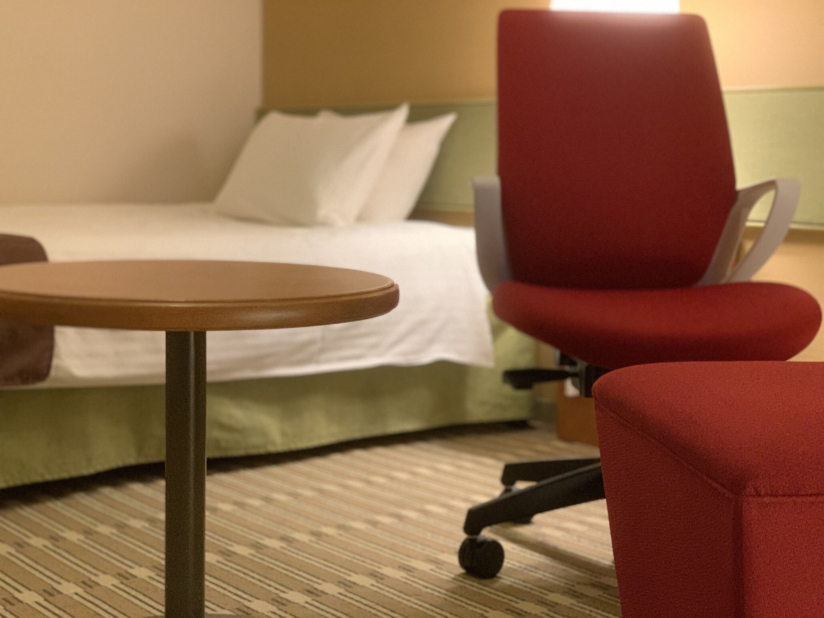 Quarto de hotel com uma cama, uma cadeira vermelha e uma pequena mesa de madeira.