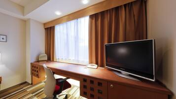 Quarto de hotel com escrivaninha de madeira, televisão, cadeira e janela com cortinas.