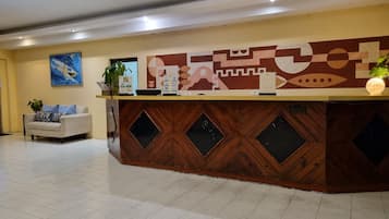Uma receção com detalhes em madeira e padrões geométricos, um sofá com almofadas estampadas e um quadro na parede.