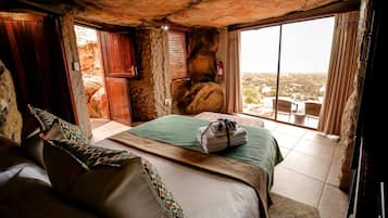 Quarto com cama, janela com vista, porta e parede de pedra.
