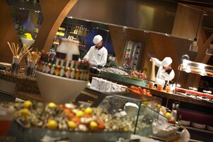 Uma área de buffet com diversos pratos, incluindo frutos do mar e legumes, e uma grande salada de frutas.