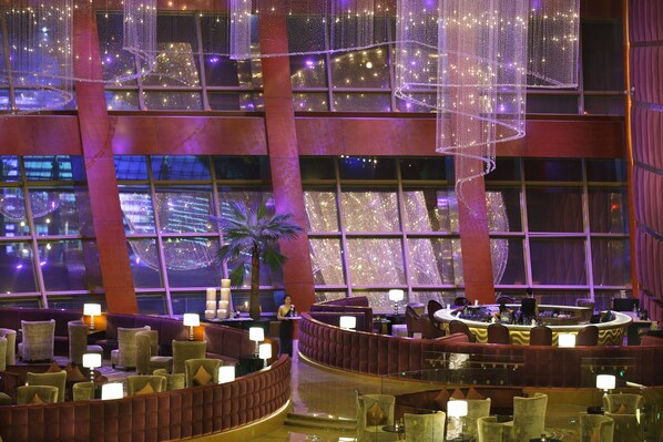 Um hall espaçoso com área de estar em curva, um bar e grandes janelas com iluminação decorativa.
