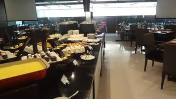 Uma área de buffet com diversos alimentos e um espaço para sentar com mesas e cadeiras.