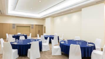 Uma sala de conferência com mesas redondas, cadeiras brancas e toalhas de mesa azuis.