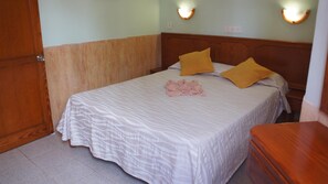 Cama bem arrumada com colcha listrada e duas almofadas, mesa de cabeceira de madeira e luminária fixada na parede.