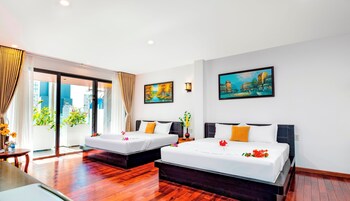 Quarto de hotel com duas camas, uma janela grande com cortinas, um quadro na parede e vista para prédios lá fora.