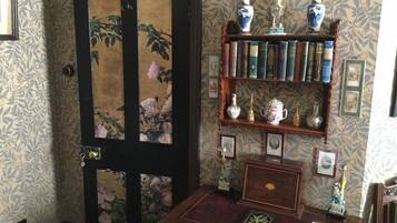 Um quarto com uma escrivaninha de madeira, uma estante com livros e objetos decorativos, e uma porta com papel de parede floral.