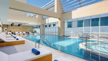 Piscina infinita no terraço com espreguiçadeiras e vista para a cidade.