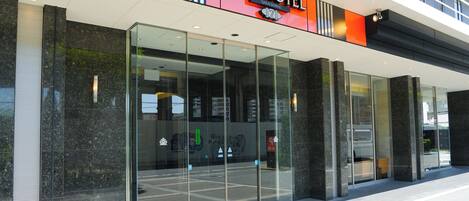 Entrada de um hotel moderno com fachada de vidro, uma placa chamativa com a inscrição