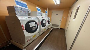 Uma lavanderia com três máquinas de lavar empilhadas, uma porta para sala privativa e um sistema de ventilação na parede.