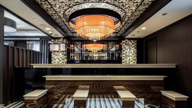 Um saguão de hotel com uma recepção central, teto trabalhado e um lustre.
