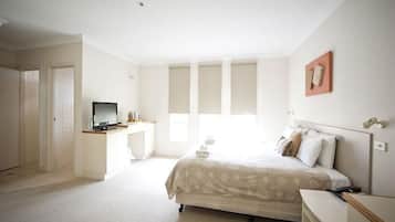 Quarto com cama, mesa de cabeceira, televisão e janela com persianas.