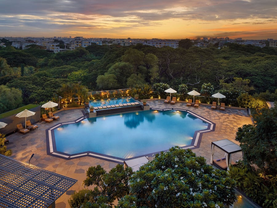 Piscina com espreguiçadeiras e guarda-sóis, cercada por vegetação e com vista para a cidade.