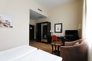 Quarto de hotel com cama, escrivaninha, computador, televisão e cadeira.