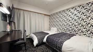 Quarto de hotel com duas camas, uma mesa, uma cadeira, uma televisão e papel de parede estampado.