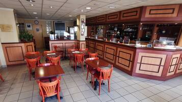 Interior de restaurante com mesas e cadeiras de madeira, área de bar e chão em mosaico.