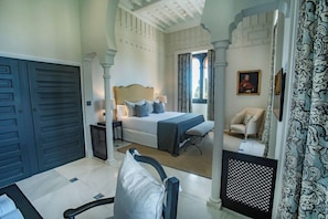 Um quarto com cama, mesas de cabeceira, uma cadeira e vista através de um arco.
