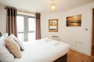 Quarto de hotel com cama, cortinas, um candelabro, um quadro e janela com vista.