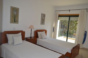 Quarto com duas camas, mesa de cabeceira, abajur e vista para o exterior.