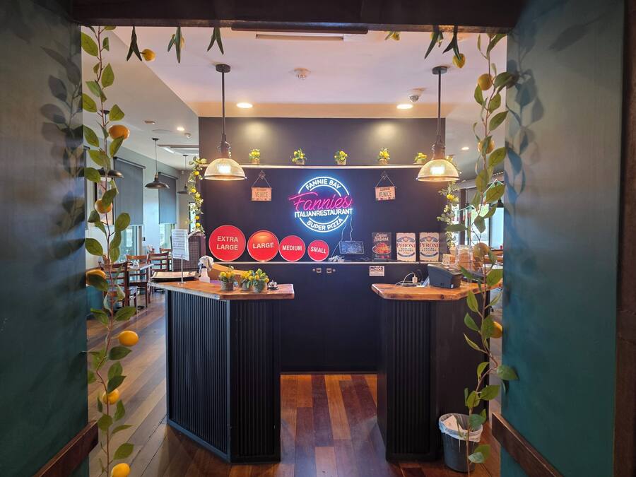 Interior de restaurante com balcão, plantas penduradas e letreiro neon.