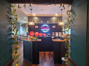 Interior de restaurante com balcão, plantas penduradas e letreiro neon.