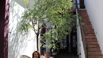 Um pátio estreito com uma escadaria, uma árvore e duas pessoas sentadas em cadeiras.