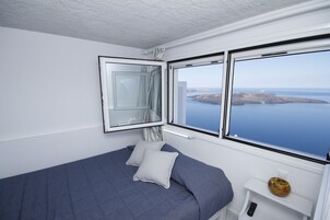 Quarto com cama, janela com vista para o mar e uma pequena prateleira com um vaso.