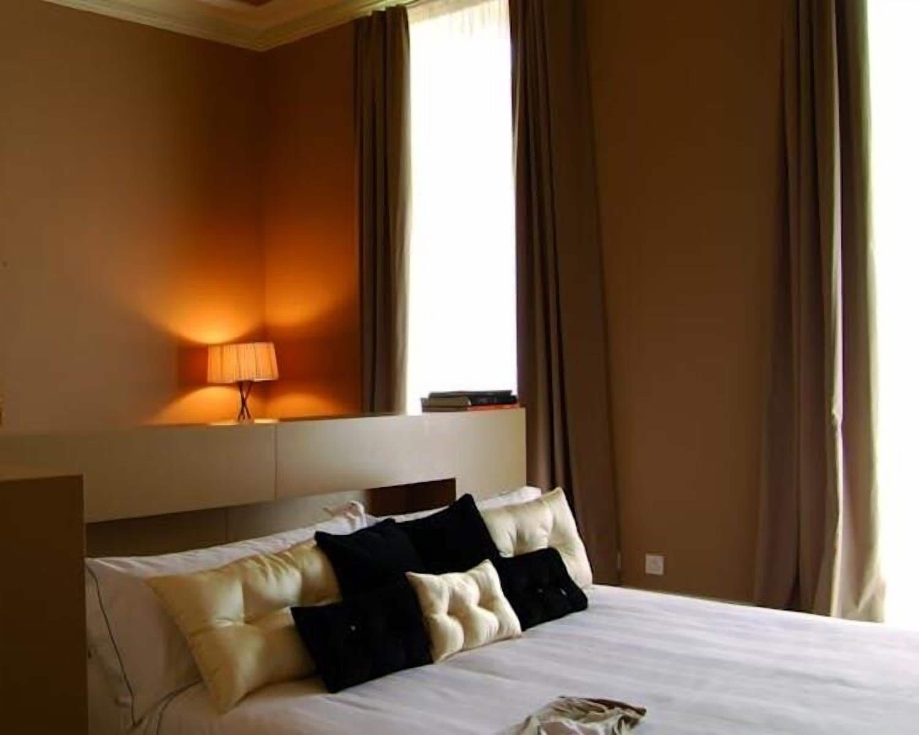 Quarto de hotel com uma cama grande, uma luminária de cabeceira e uma janela com cortinas.