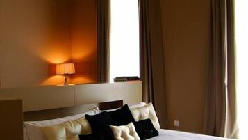 Quarto de hotel com uma cama grande, uma luminária de cabeceira e uma janela com cortinas.