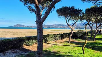 Paisagem costeira com praia, árvores e montanhas ao longe.