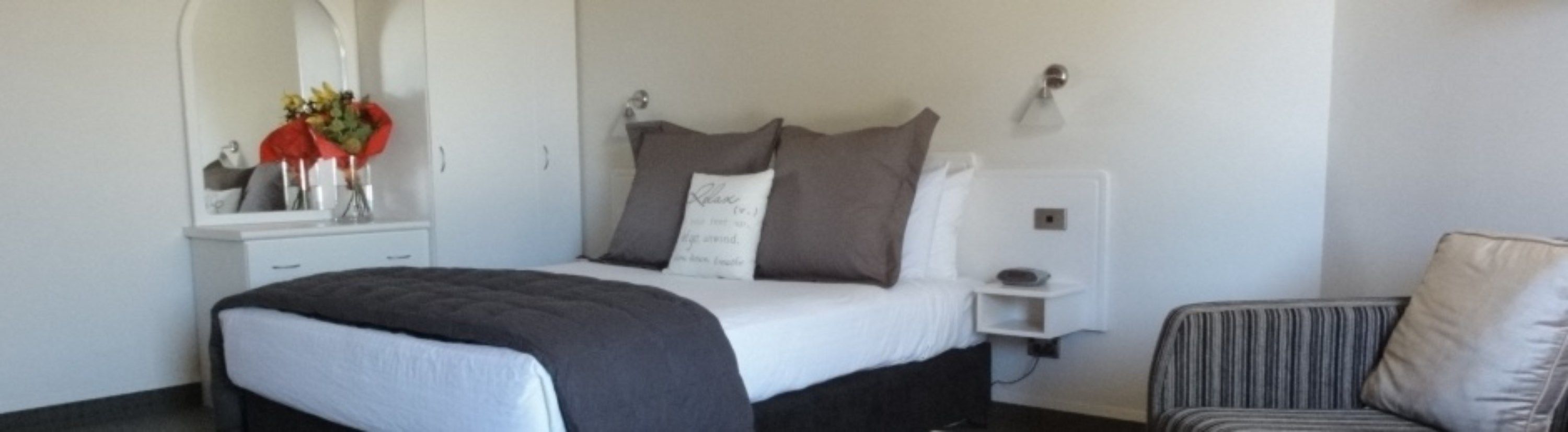 Quarto com cama, mesa de cabeceira, luminária e uma cadeira.
