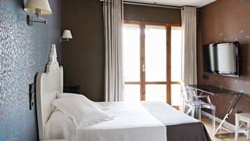 Quarto de hotel com cama, televisão, escrivaninha com cadeira e janela com cortinas.