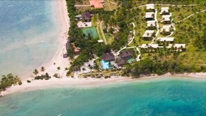 Vista aérea de um resort costeiro com praia, piscina e diversas acomodações no estilo de bangalô.