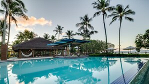 Uma piscina com estrutura de telhado de palha, palmeiras e céu claro.