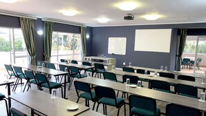 Uma sala de conferências com mesas, cadeiras, um projetor e um quadro branco.
