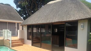 Uma casa com piscina, telhado de palha e porta de correr de vidro que dá para um espaço de varanda coberto.