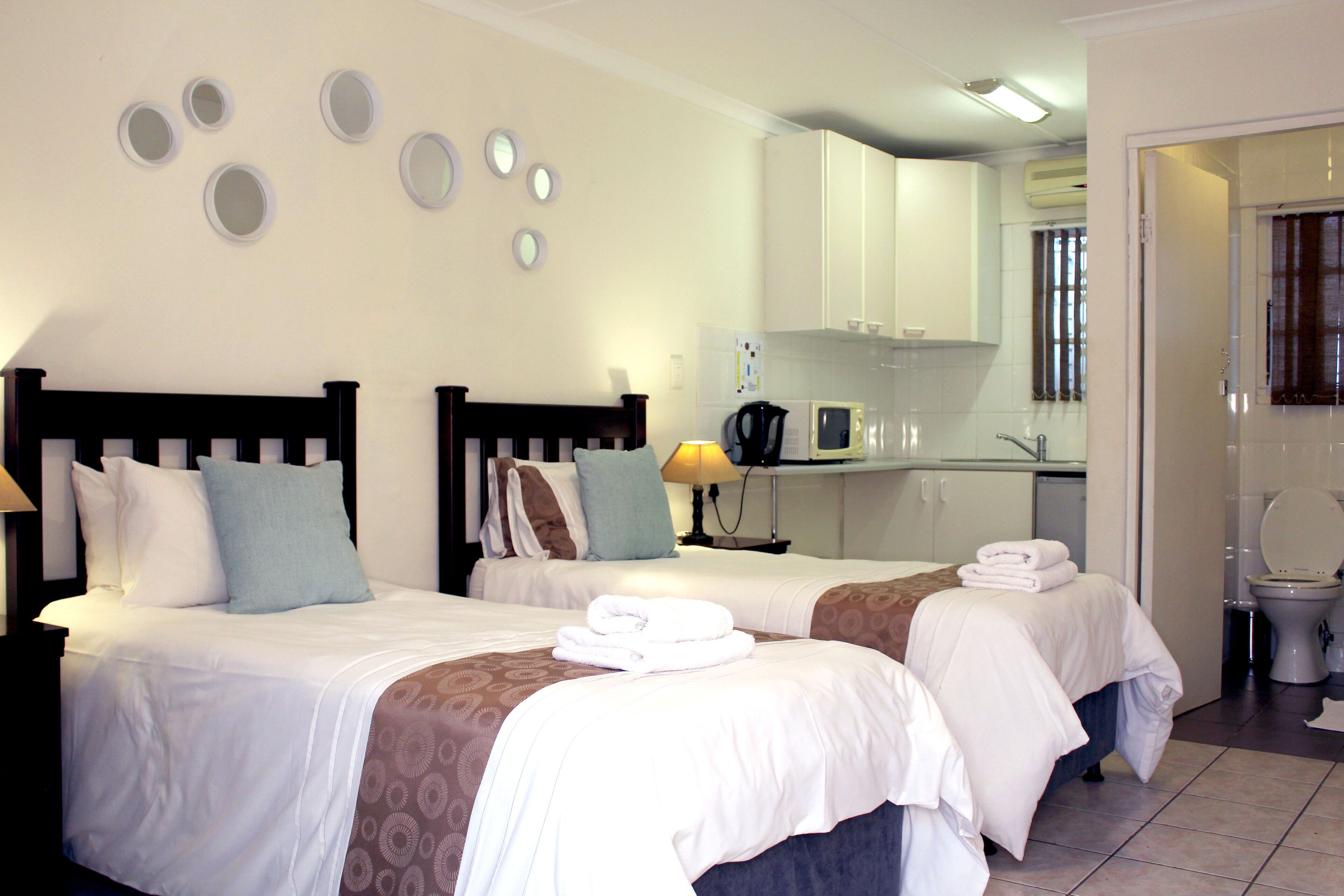 Quarto de hotel com duas camas, uma kitchenette pequena, um banheiro e um espelho.