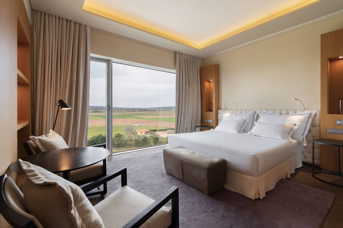 Quarto de hotel com uma cama grande, uma mesa, uma cadeira e vista para o campo.