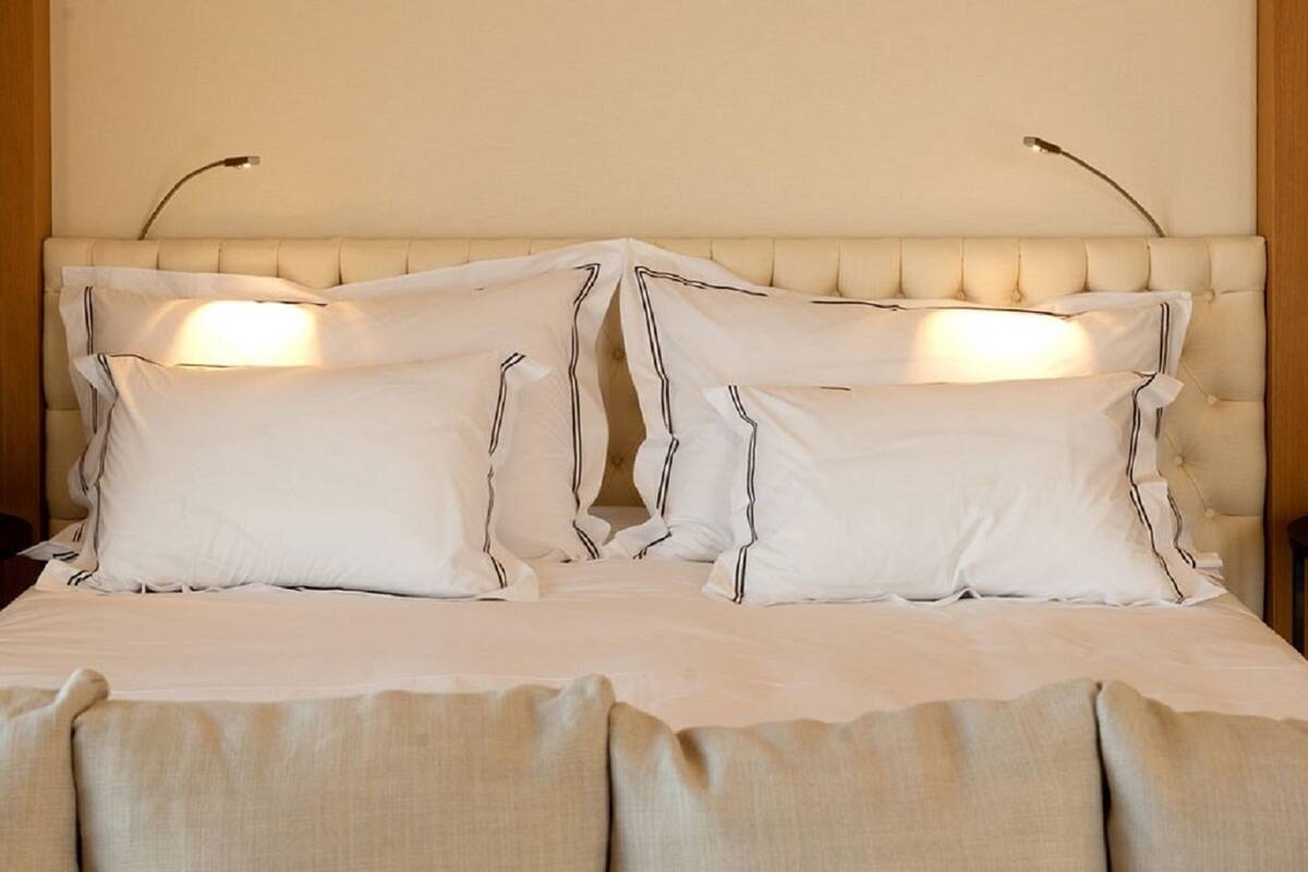 Uma cama com cabeceira estofada, duas almofadas e uma luminária de cabeceira.